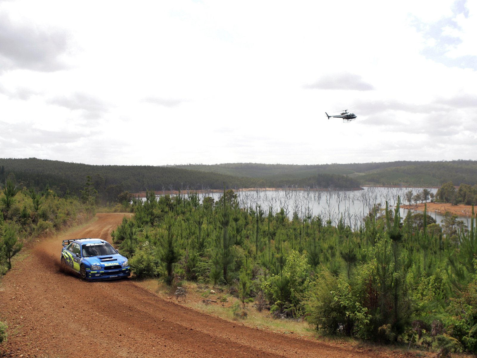 Rallye Rush at Lake Bled: Race Car and Helicopter in Forest HD Wallpaper